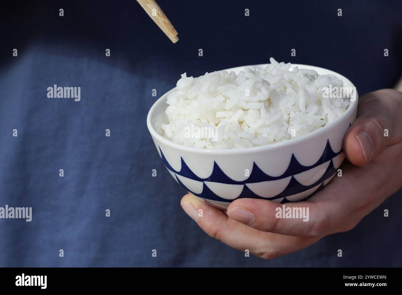Closeup up of male Caucasian's hand holding bowl of cooked white rice ...