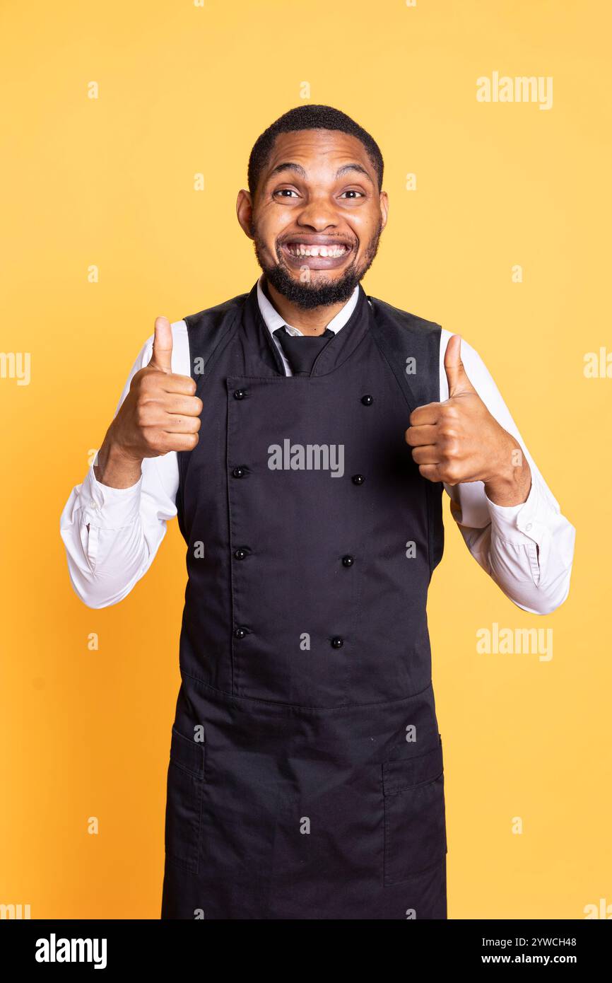Pleased waiter showing a thumbs up symbol in front of the camera, presenting his approval and ...