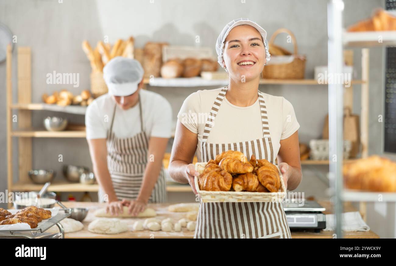 Smiling female baker in uniform stands behind counter in small private ...