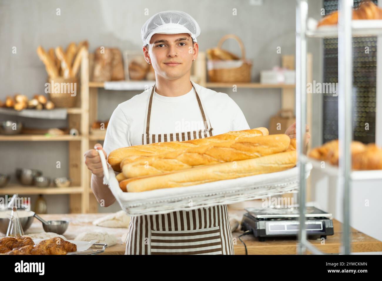 Happy male baker posing with basket of freshly baked baguettes in ...