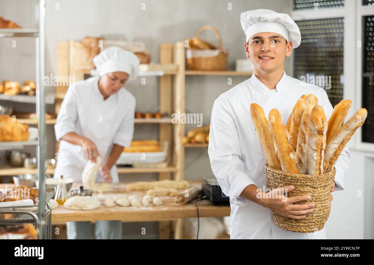 Happy male baker posing with basket of freshly baked baguettes in ...