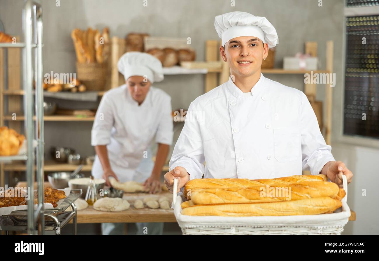 Happy male baker posing with basket of freshly baked baguettes in ...
