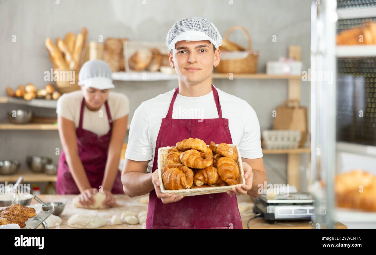 Successful young baker presenting golden croissants in inviting bakery ...
