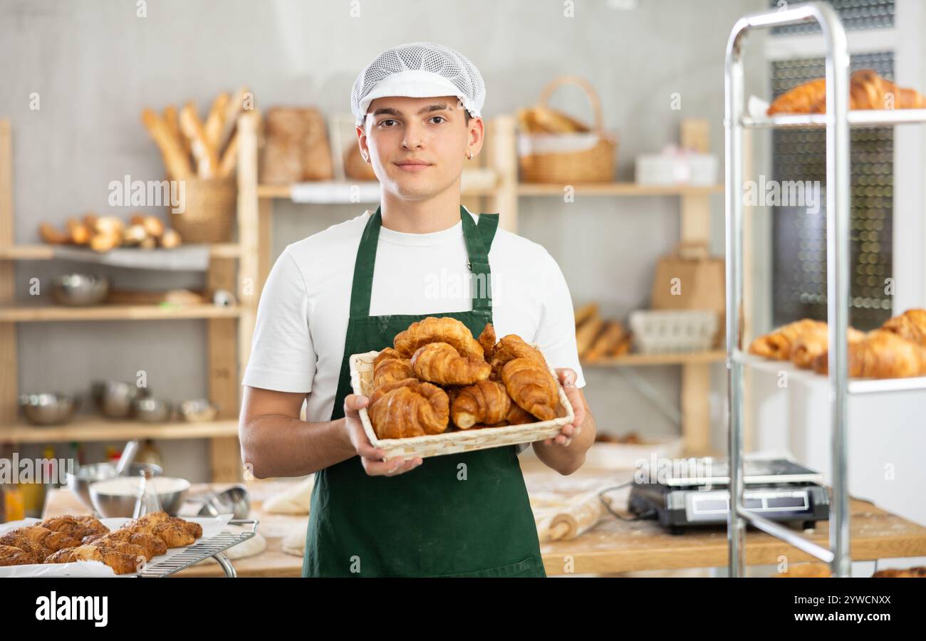Positive male baker in uniform stands behind counter in small private ...