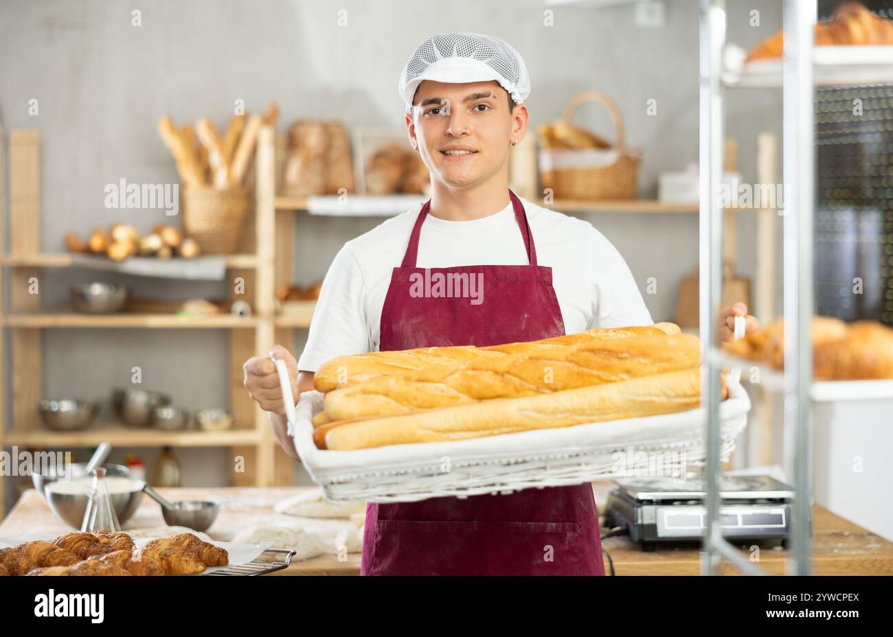 Happy male baker posing with basket of freshly baked baguettes in ...