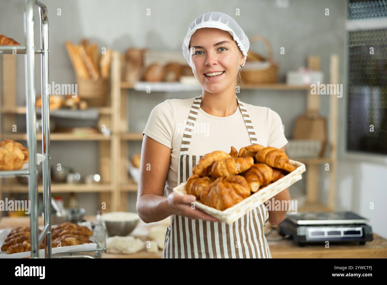 Cheerful young female artisan baker presenting fluffy croissants in bakery Stock Photo - Alamy