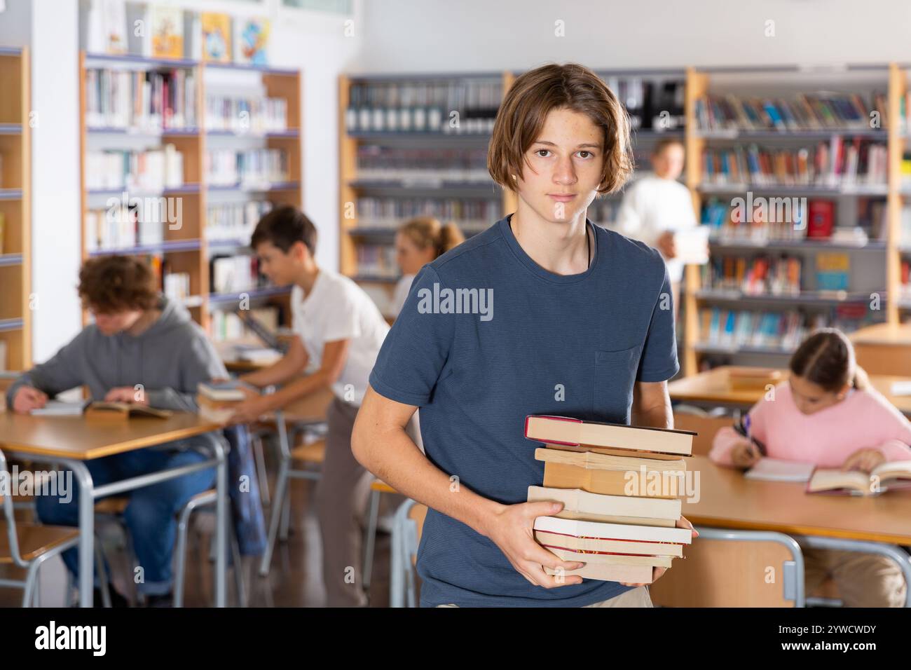 Boy with pile of books in library Stock Photo - Alamy