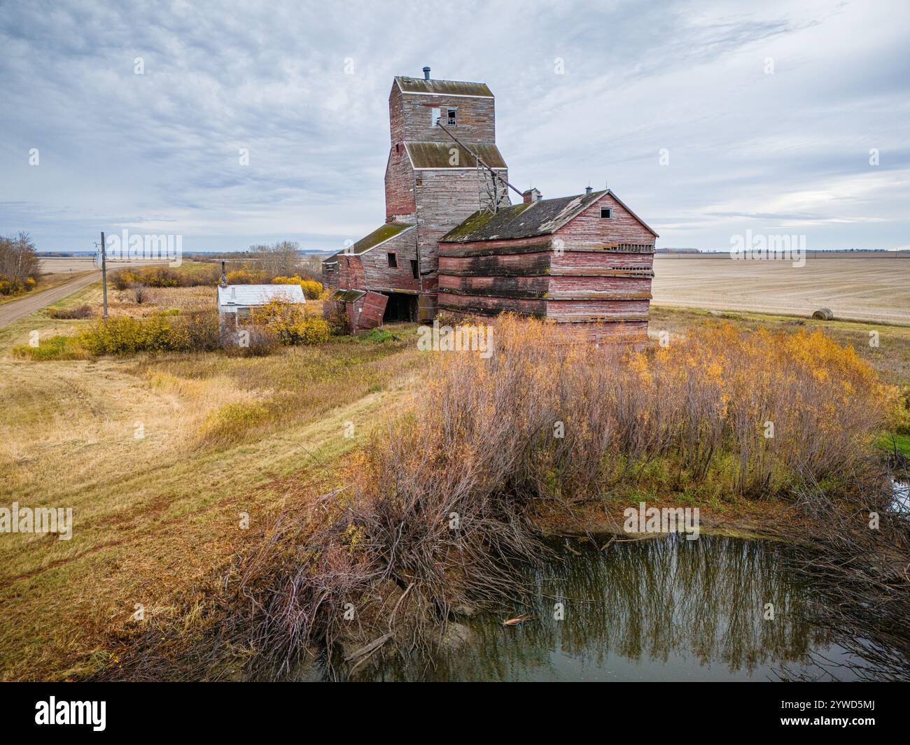 A large, old building sits in a field with a pond in front of it. The ...