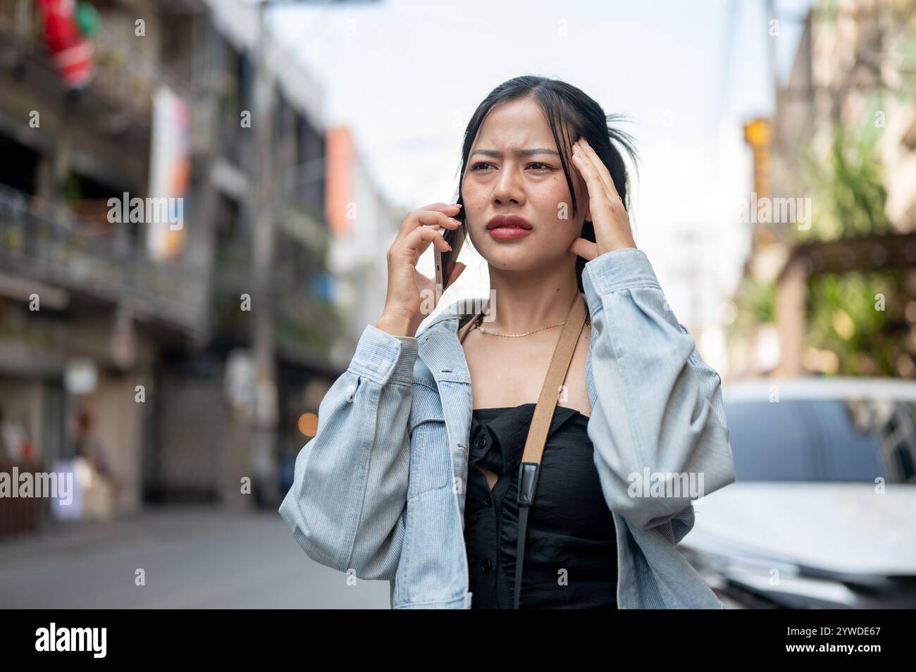 A confused Asian female tourist in a denim jacket talking on the phone ...