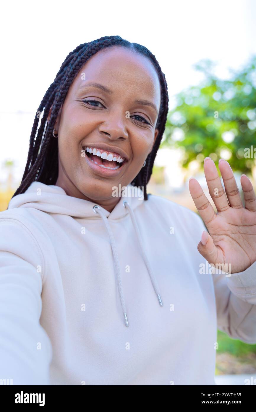 Smiling woman waving at camera during an outdoor video call.Vertical ...