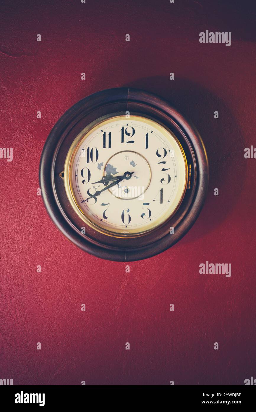 A vintage-style wall clock with distinct numbers rests on a vibrant red ...