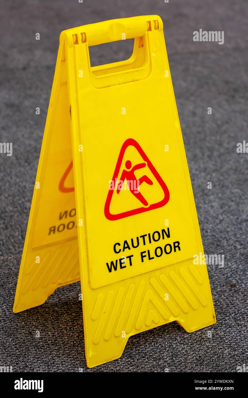 A bright yellow sign displays a caution notice about a wet floor Stock ...