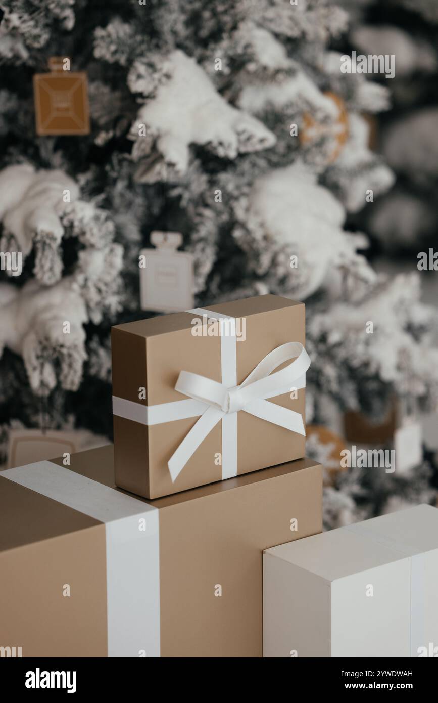 A gift box under a snow-covered Christmas tree tied with a white ribbon ...
