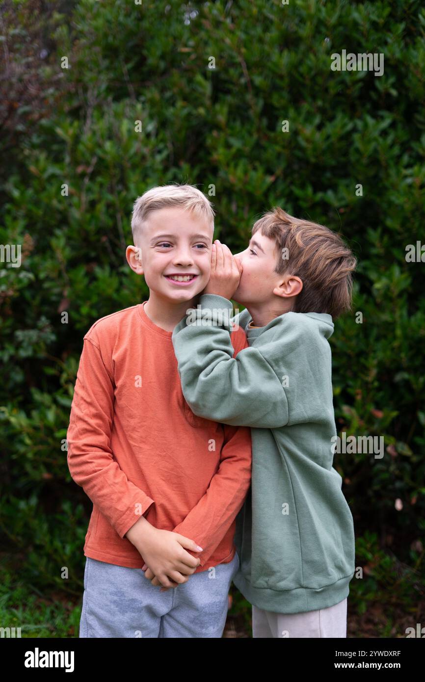 Two young boys sharing a secret in a playful moment, whispering and ...