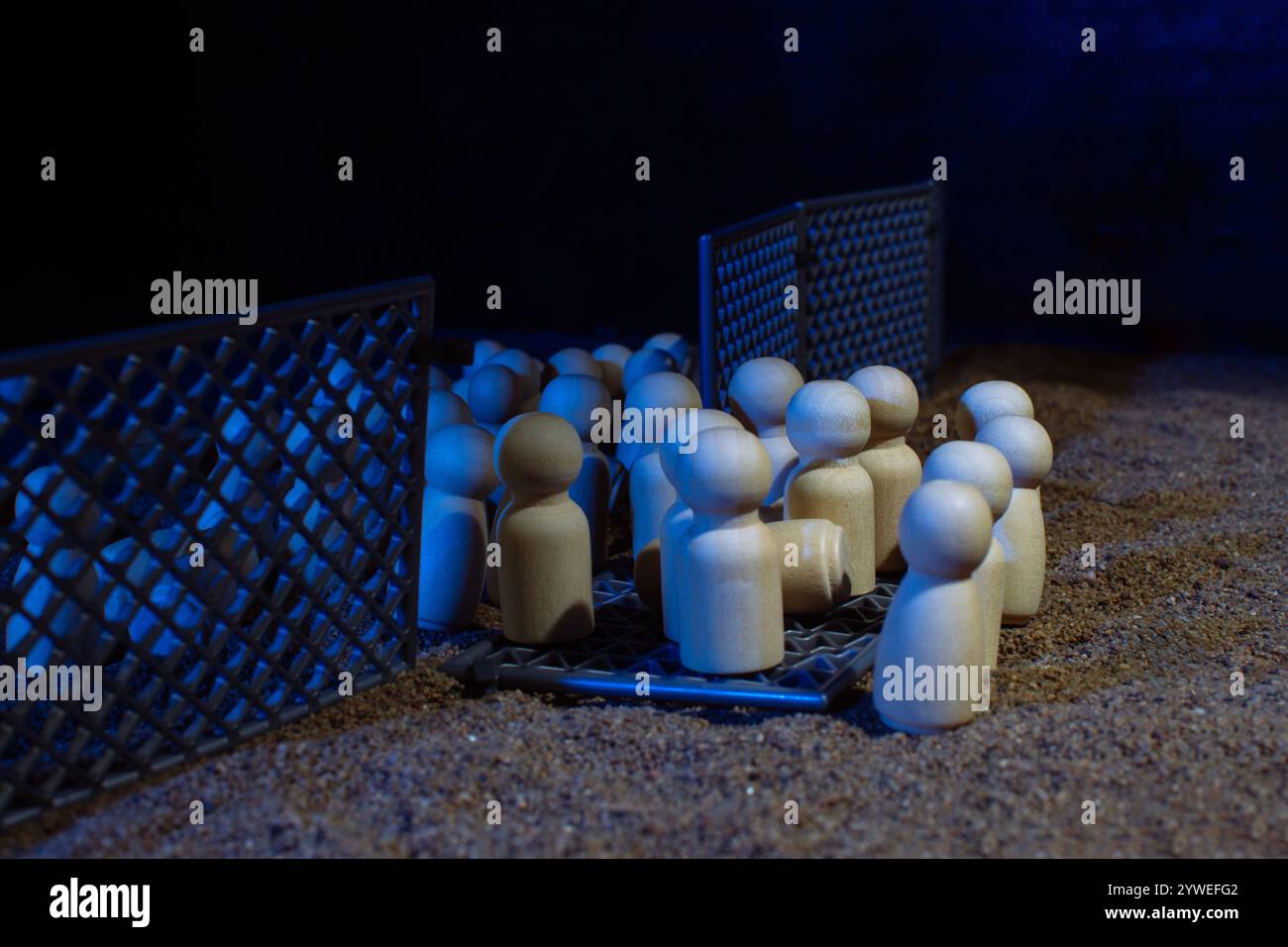 Wooden figures behind a fence on sand, symbolizing borders and ...