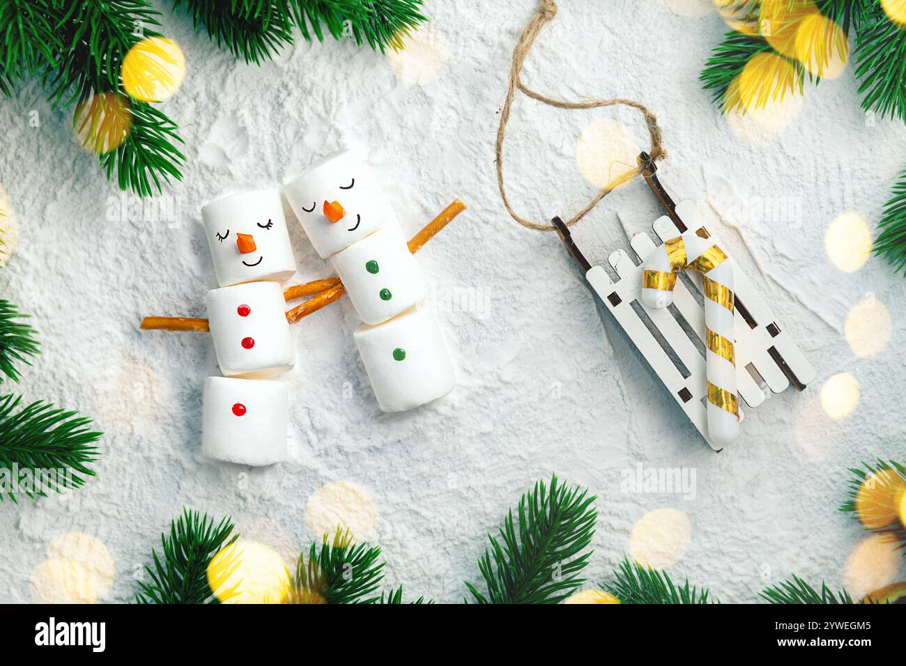 Funny marshmallow snowmen holding hands lying on snow near christmas ...