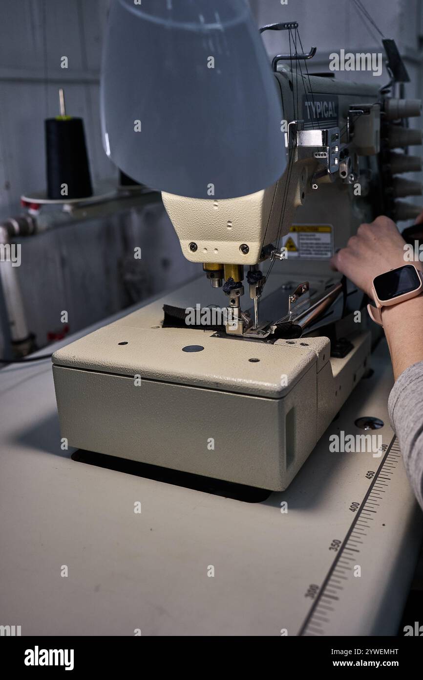 A worker's hands guide fabric through an industrial sewing machine in a ...