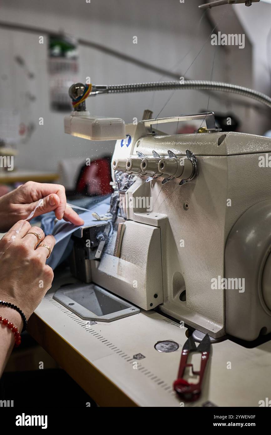 A skilled worker operates an industrial overlock machine, demonstrating ...