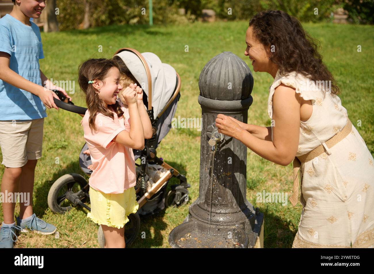 A joyful family with children have fun around a water fountain in a ...