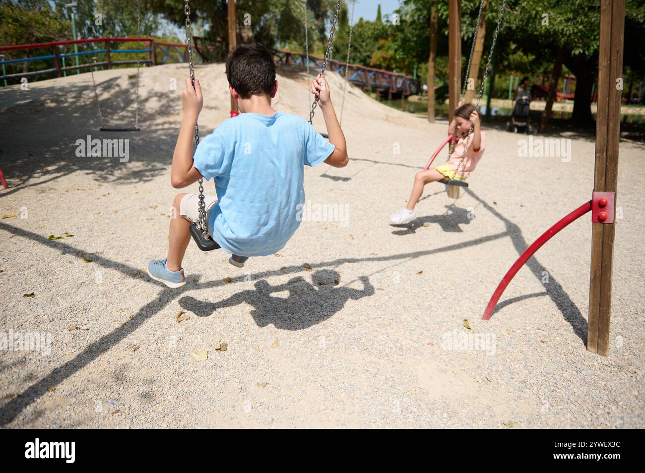 Two children swinging joyfully on swings in a sunny park setting, enjoying playtime Stock Photo ...