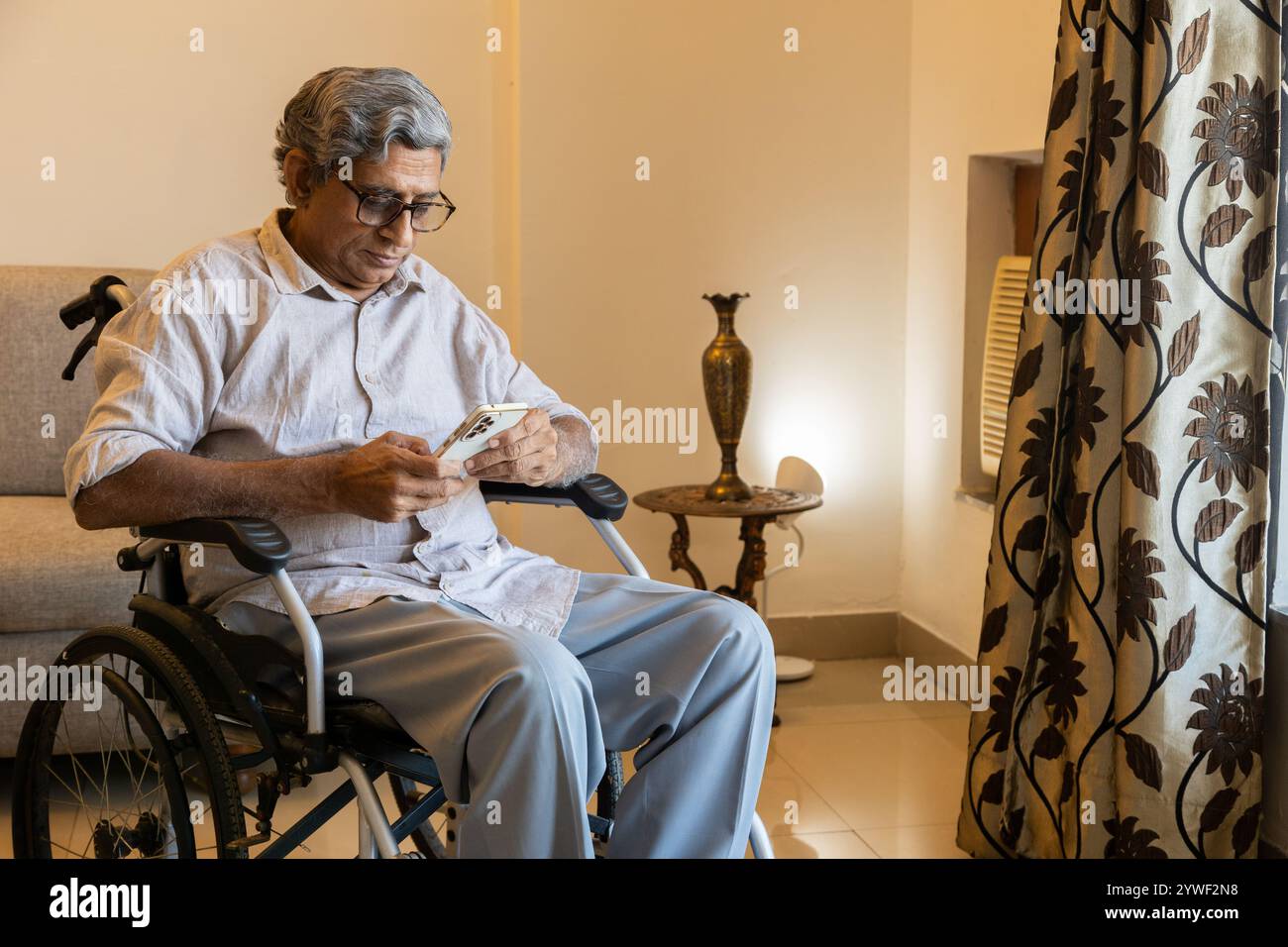 Indian senior disabled man using smart phone sitting on wheel chair at ...