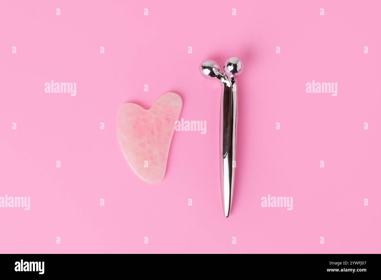 Top view of trendy face tools roller and quartz gua sha on pastel pink ...