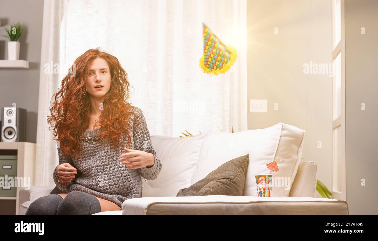 Young woman with long red curly hair sitting on a white sofa, looking ...