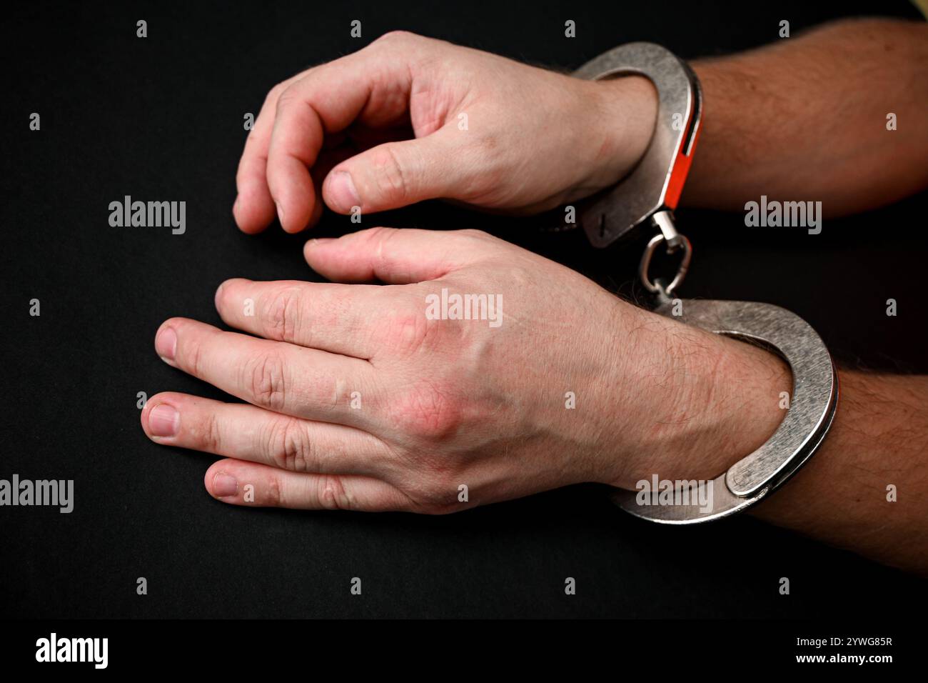 Handcuffed man showing his wrists on a dark background Stock Photo - Alamy