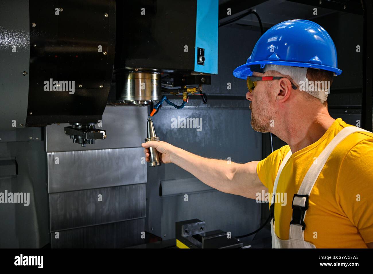 Metalworker is changing the drill bit in a cnc machine during a metal ...