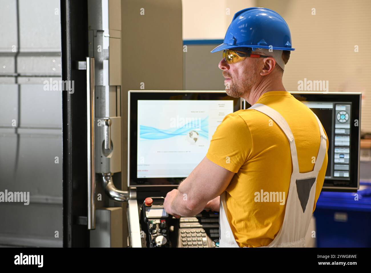 Metalworker wearing safety glasses and hardhat using cnc milling ...