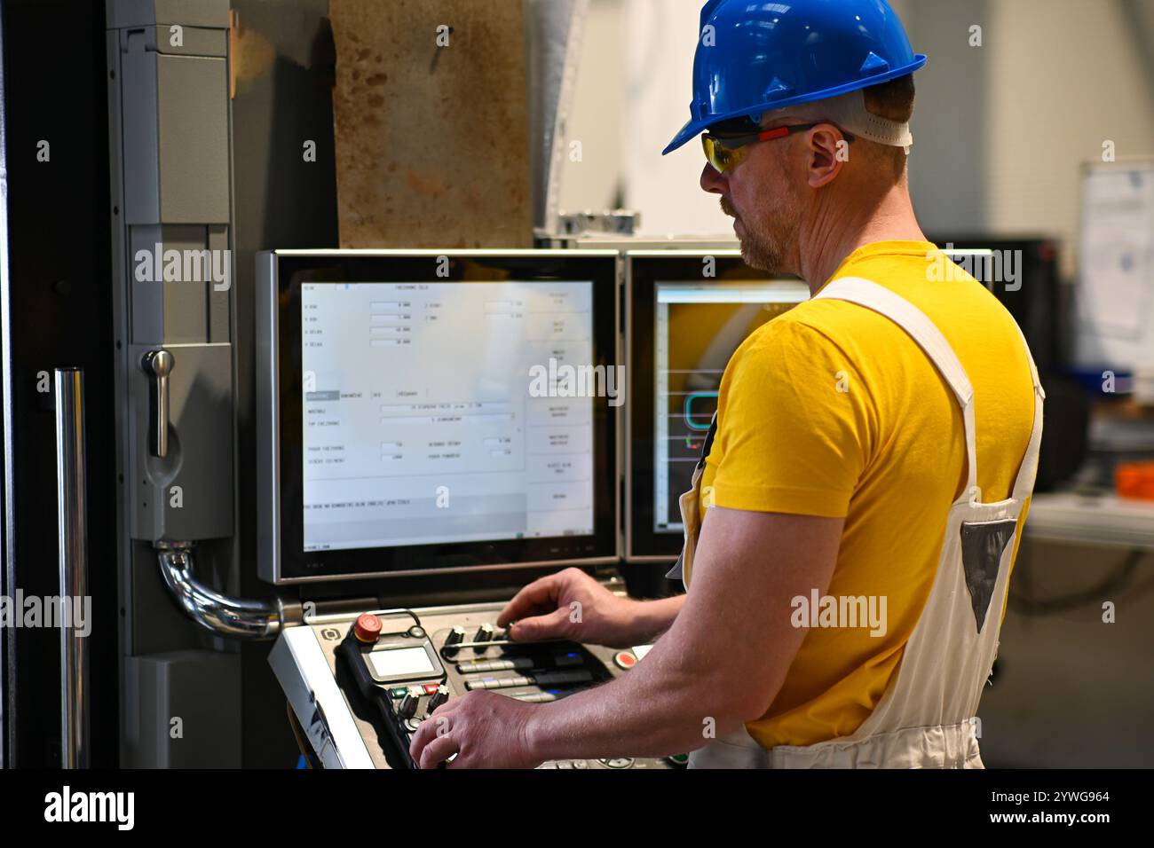 Metalworker wearing safety glasses and hardhat using cnc milling ...