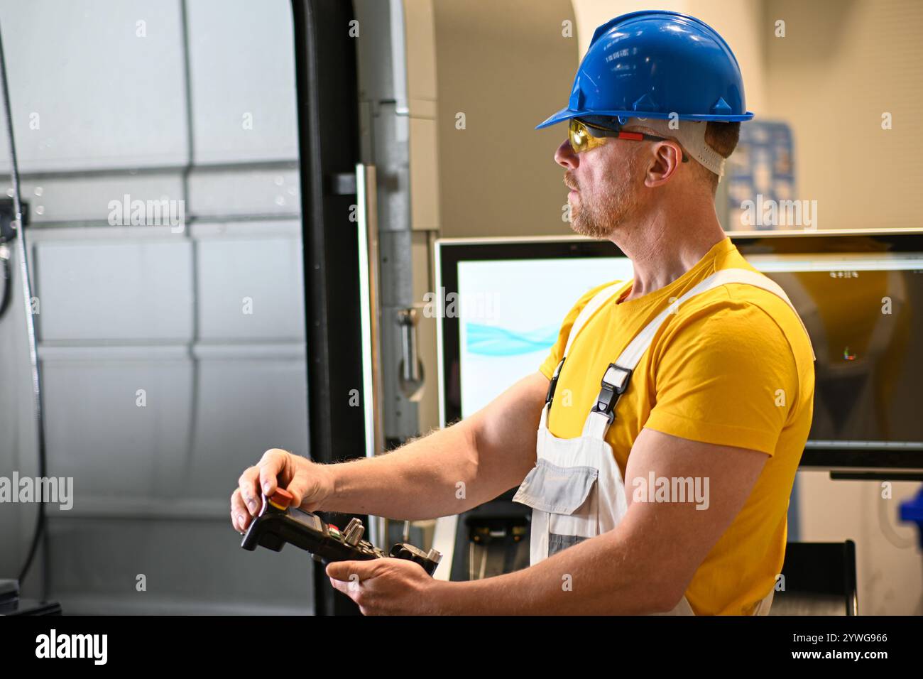 Factory worker wearing safety equipment operating industrial machinery ...
