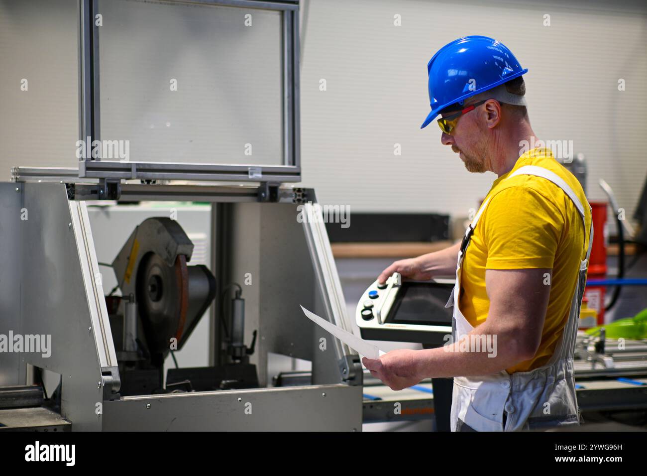 Factory worker wearing safety glasses and hardhat operating industrial ...