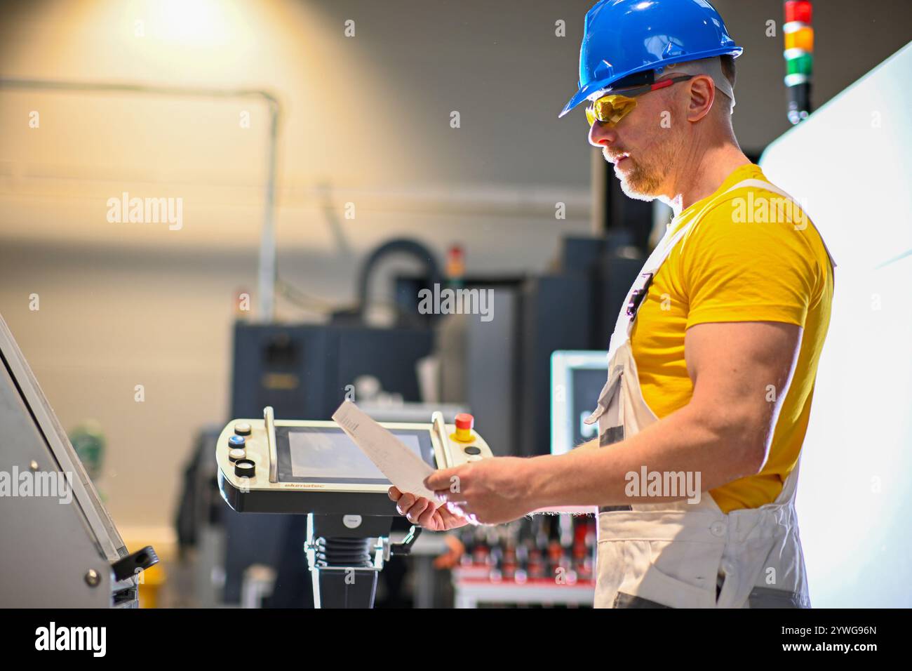 Factory worker wearing safety glasses and hardhat operating industrial ...