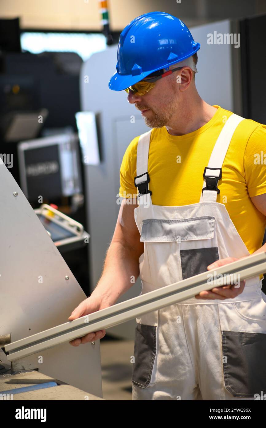 Factory worker operating machinery and holding a metal part, wearing ...
