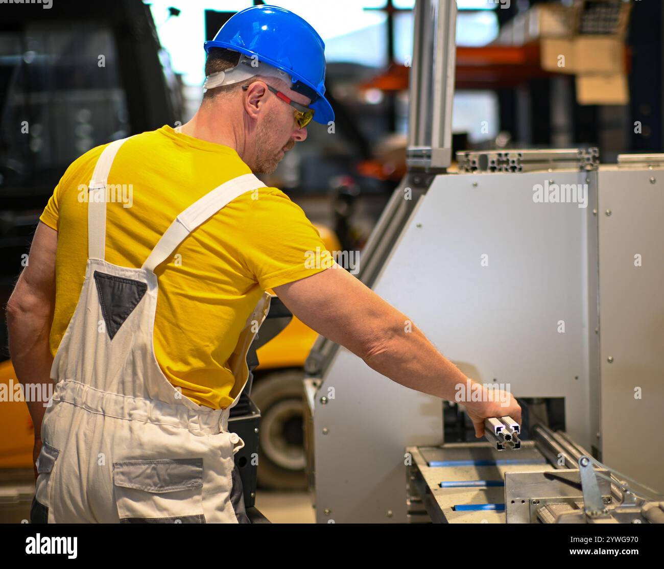 Factory worker operating machinery and holding a metal part, wearing ...