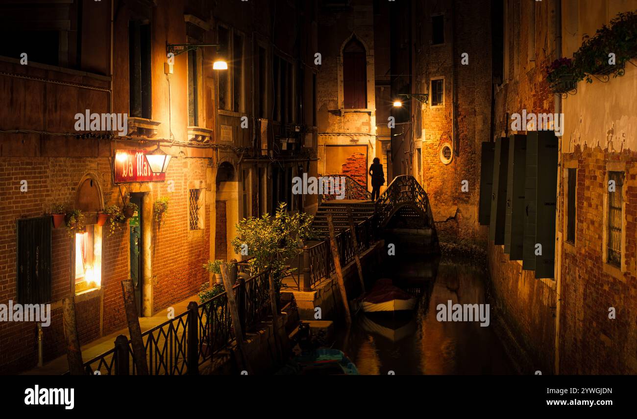 Evening stroll along narrow canal in historic Venice with dim street ...