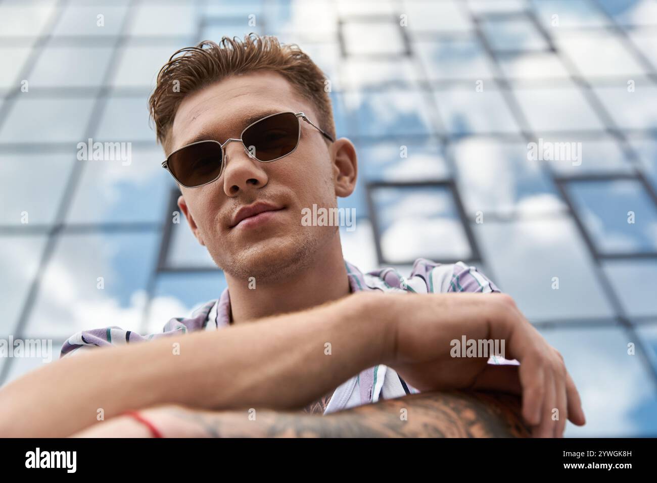 Young man poses confidently beside a reflective glass building Stock ...