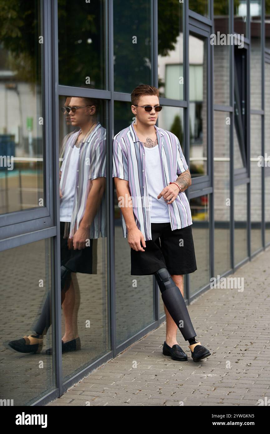 A young man with a prosthetic leg leans against glass windows ...