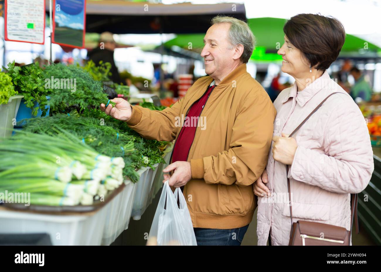 Positive mature male and female picking dill at local grocery bazaar ...