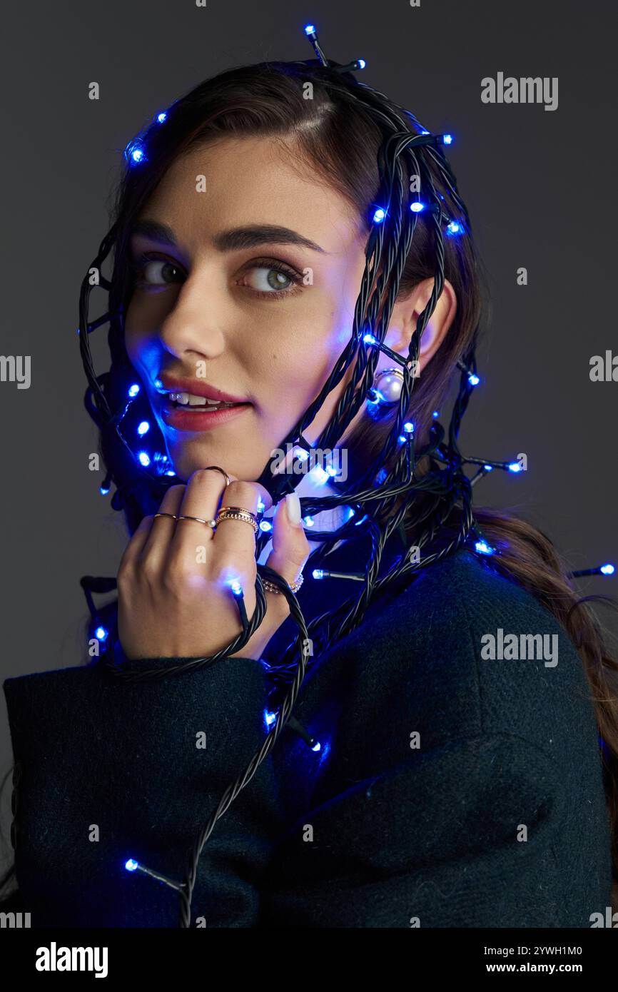 A pretty young woman playfully wraps herself in blue string lights, showcasing her creativity ...