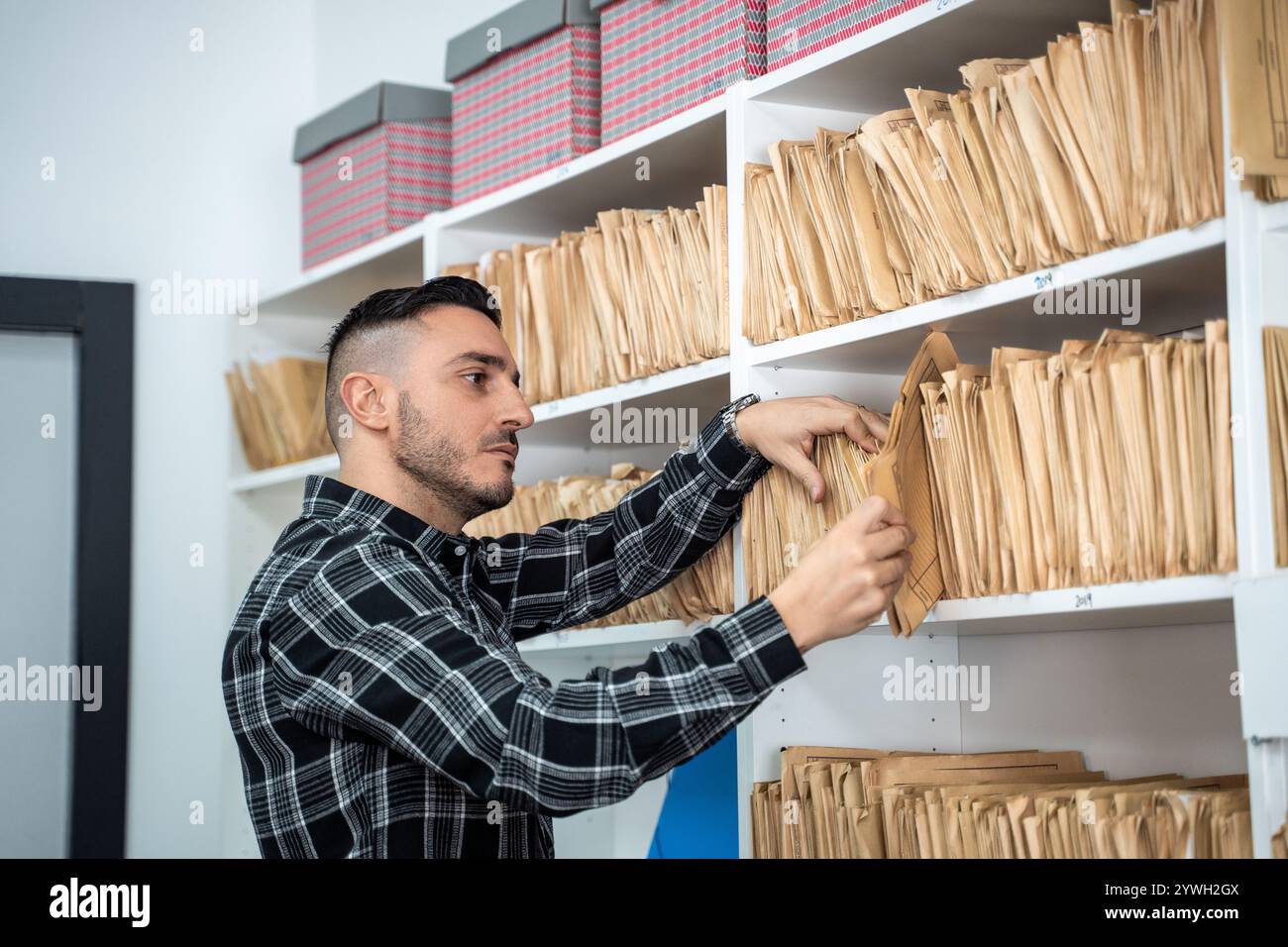 Young office worker searching files in archive room, organizing documents on shelves, storing ...