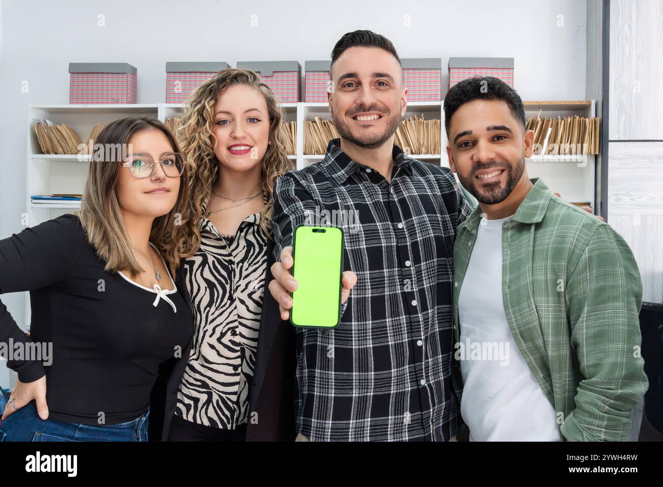 Four smiling colleagues showing a smartphone with green chroma key ...