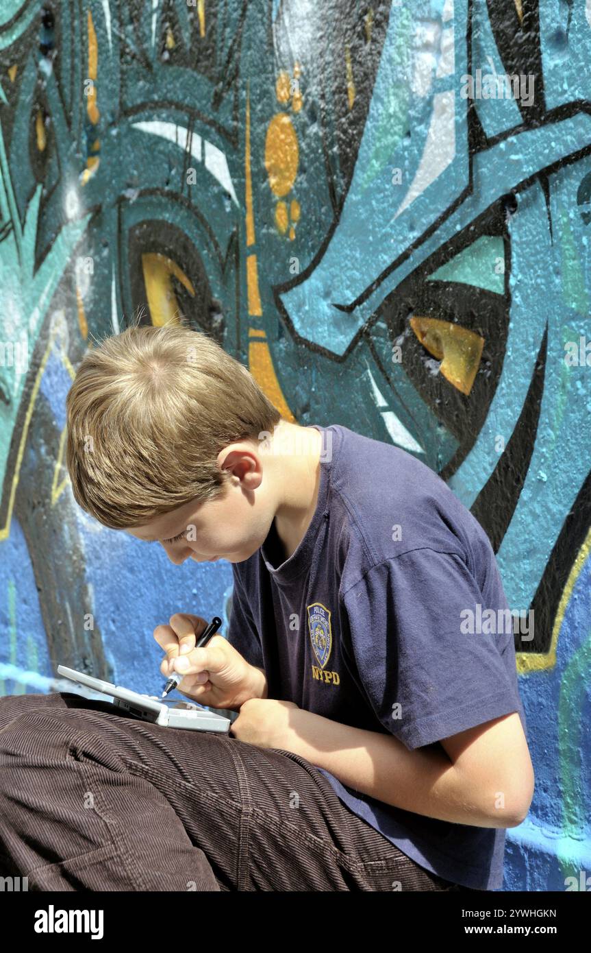 Ten-year-old boy playing with his Nintendo in front of a graffiti wall ...