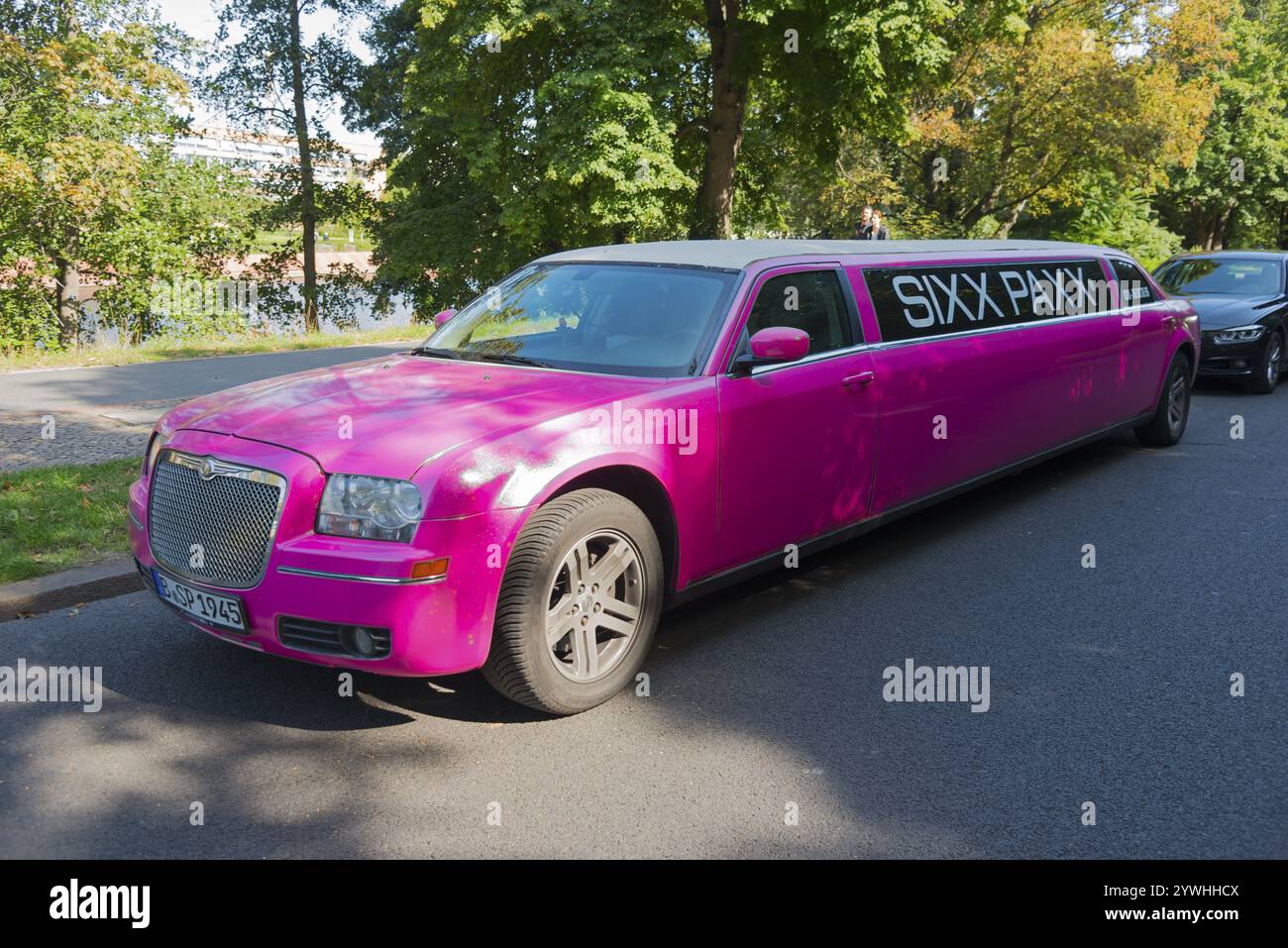 An eye-catching pink limousine parked on the roadside under trees in ...