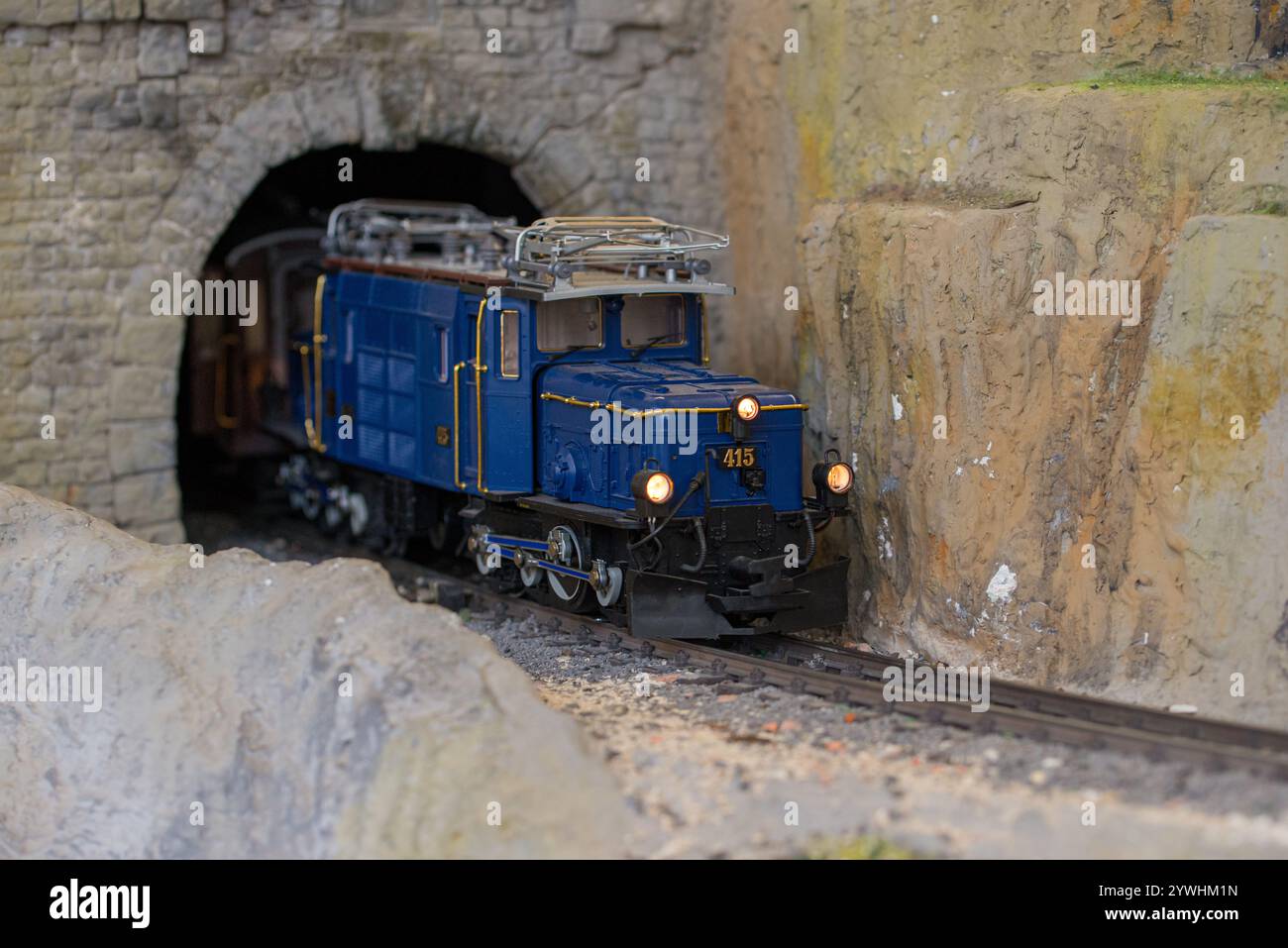 Blue model train exits stone tunnel during daytime model railroad ...