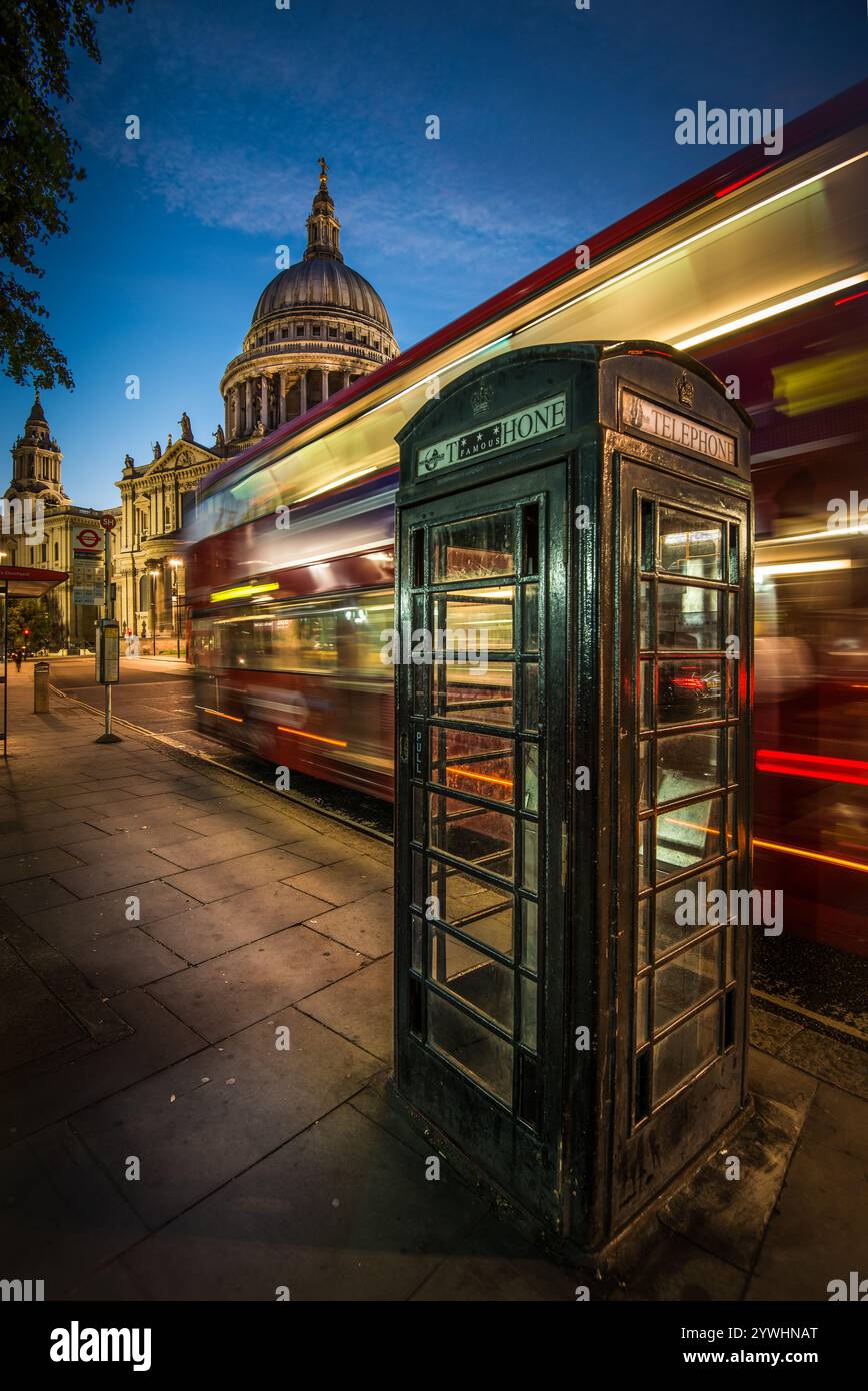 London phone booth stands still as buses rush by under evening sky near ...
