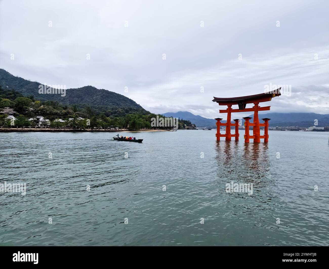 The vibrant red torii gate stands in the water, contrasting with green ...