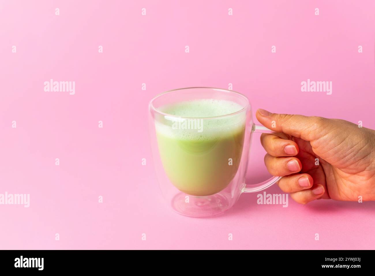 Hand holding a glass cup of matcha latte with a foam on light pink ...