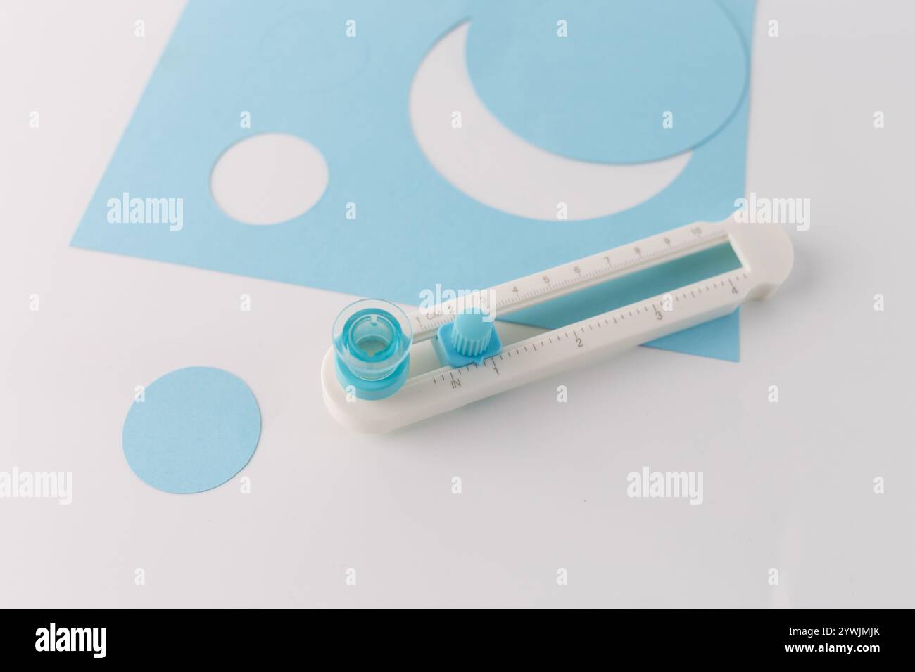 Paper circle cutter tool with blue cutouts on a white background. Close ...
